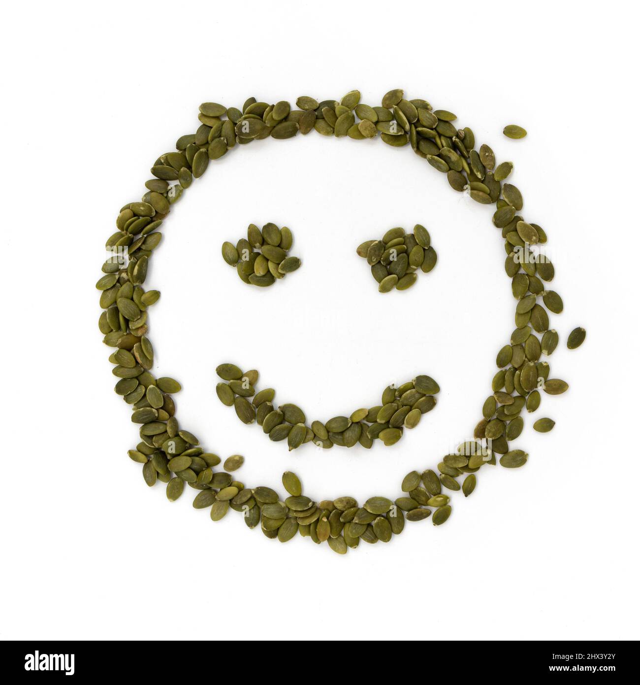 green pumpkin seeds in the shape of smiling face on white background ...