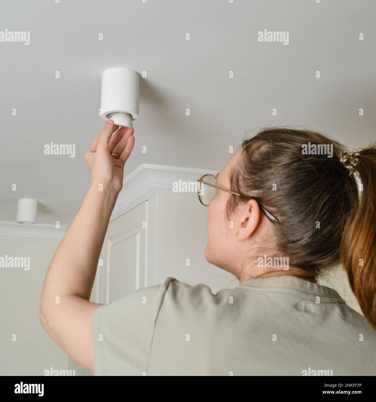 A woman changes a ceiling energy saving light bulb with LED light lamp ...