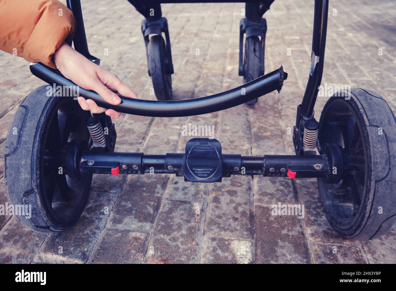 A woman hand holds a broken baby carriage chassis. Damage to the ...
