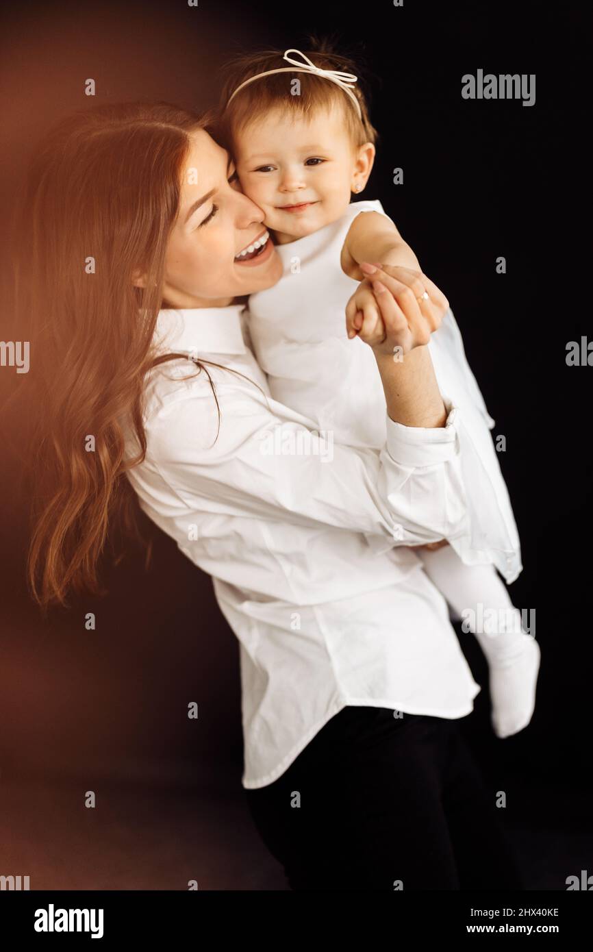 Happy brunette woman gently hugging beautiful baby girl, smiling. Attractive young mother ...