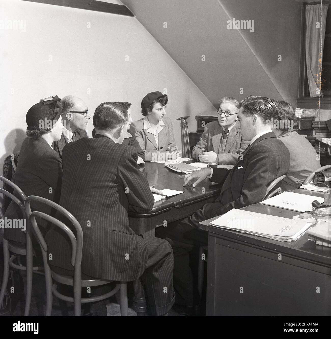 1950s, England. Small group of men and women having a business meeting ...