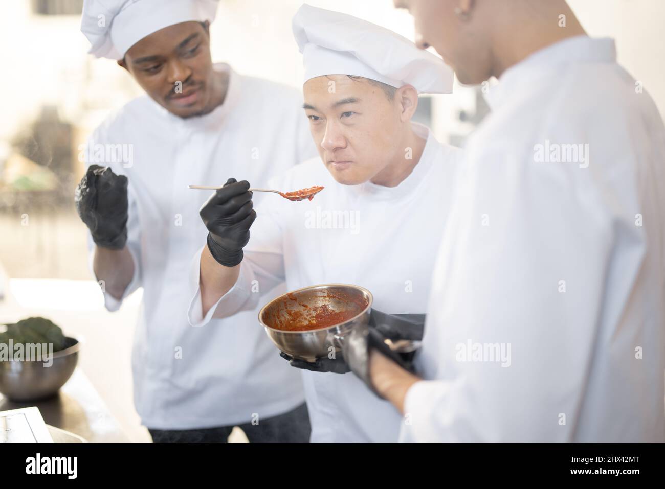 Three chef cooks with different ethnicities tasting sauce with a spoon ...