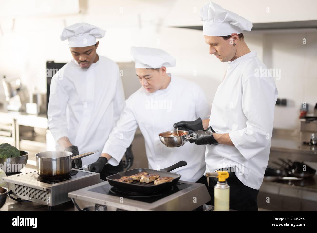 Three chef cooks with different ethnicities tasting sauce with a spoon ...