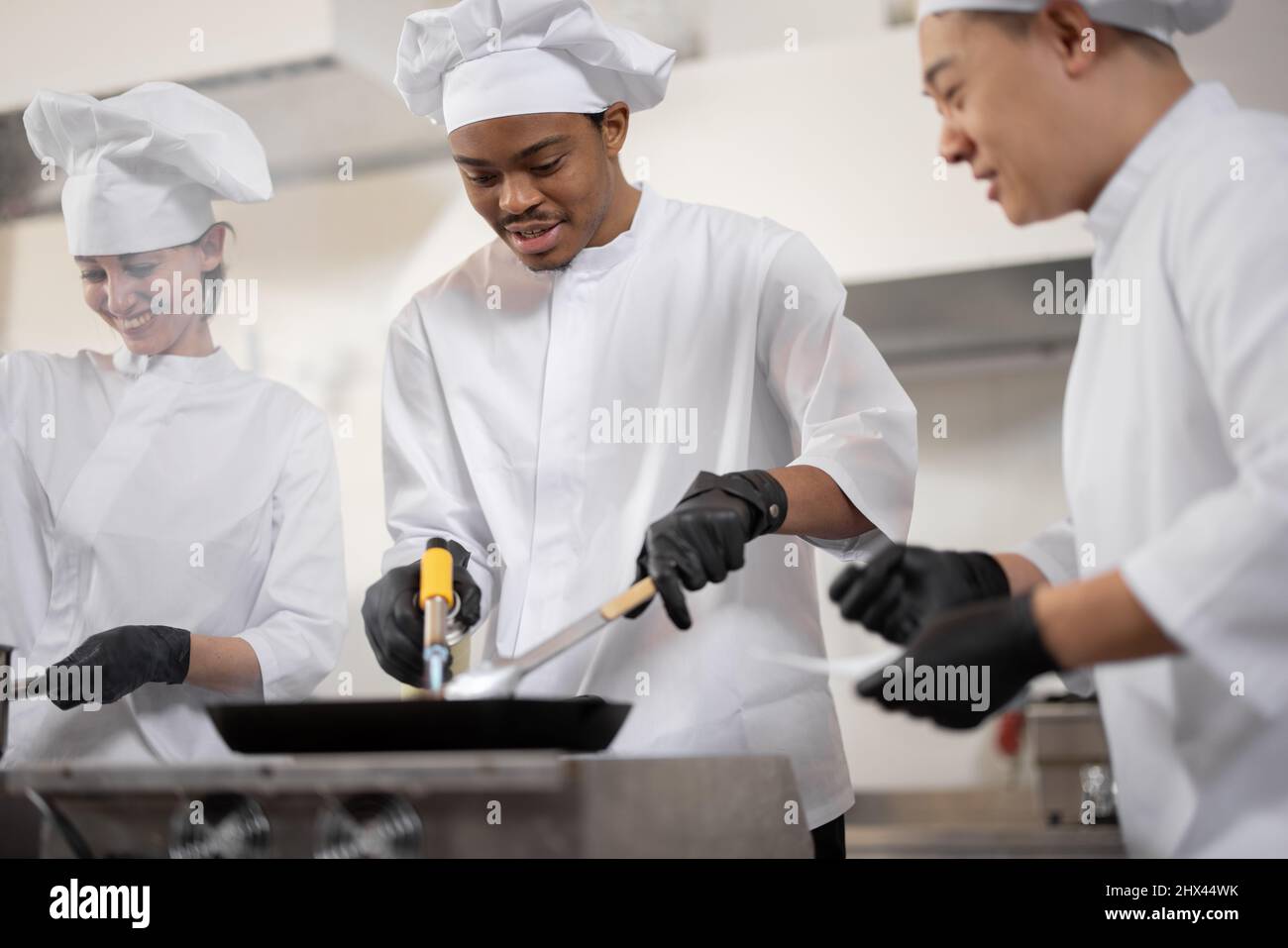 Multiracial team of professional cooks in uniform preparing meals for a ...