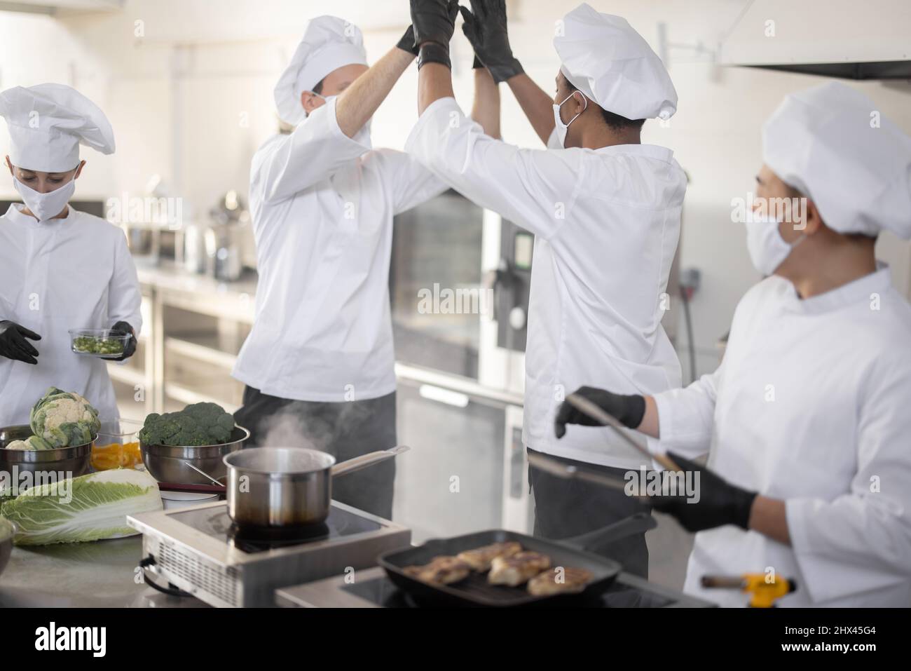 Multiracial team of cooks giving five with hands each other, while ...