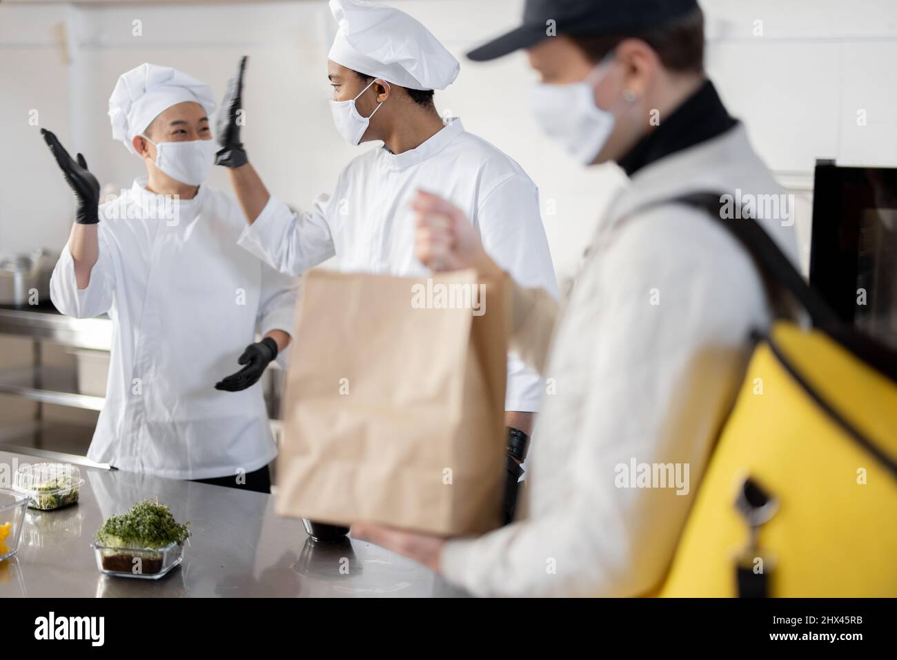 Courier waiting for an order for delivery in the kitchen with chefs ...