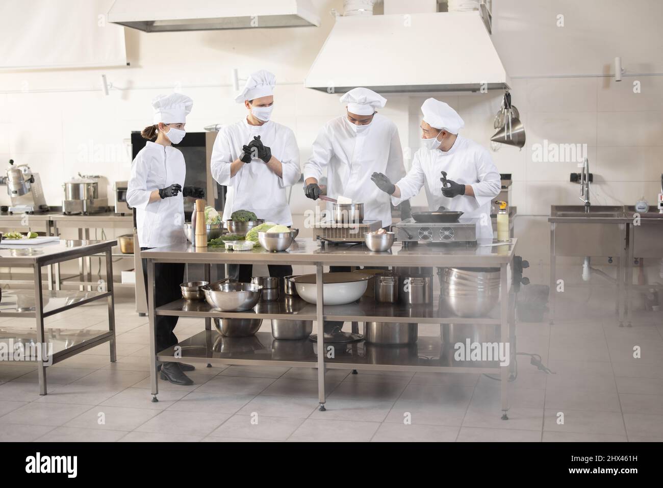 Multiracial team of cooks in white uniform cooking together in ...