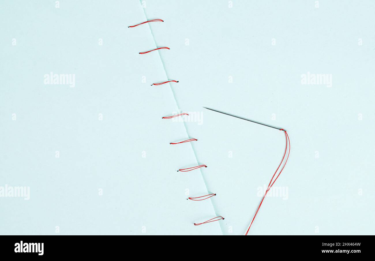 Two pieces of torn paper sewn together with a red string, financial ...