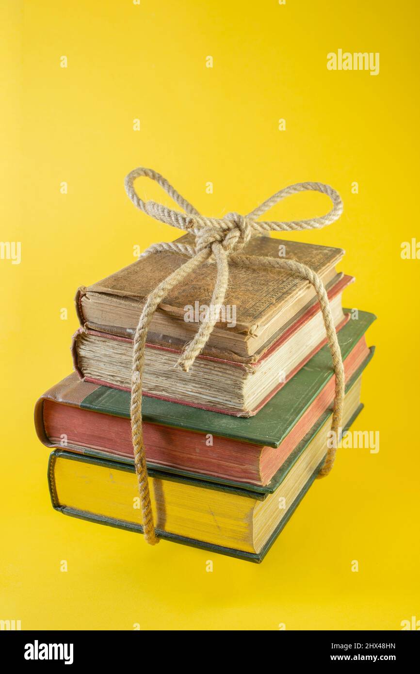 4 stacked books tied with a jute rope levitating on yellow background ...
