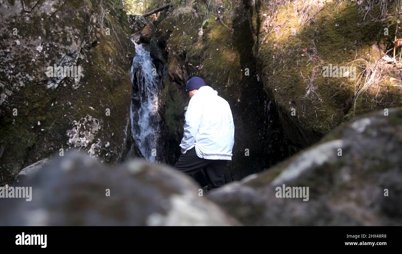 Rear view of a man in white jacket going down to the waterfall in gorge ...