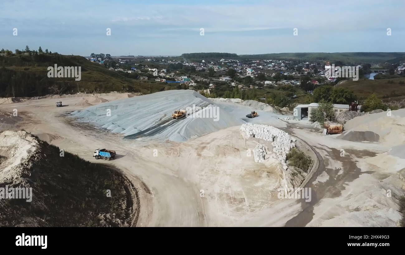 Flying above stone quarry with working heavy trucks and machines ...