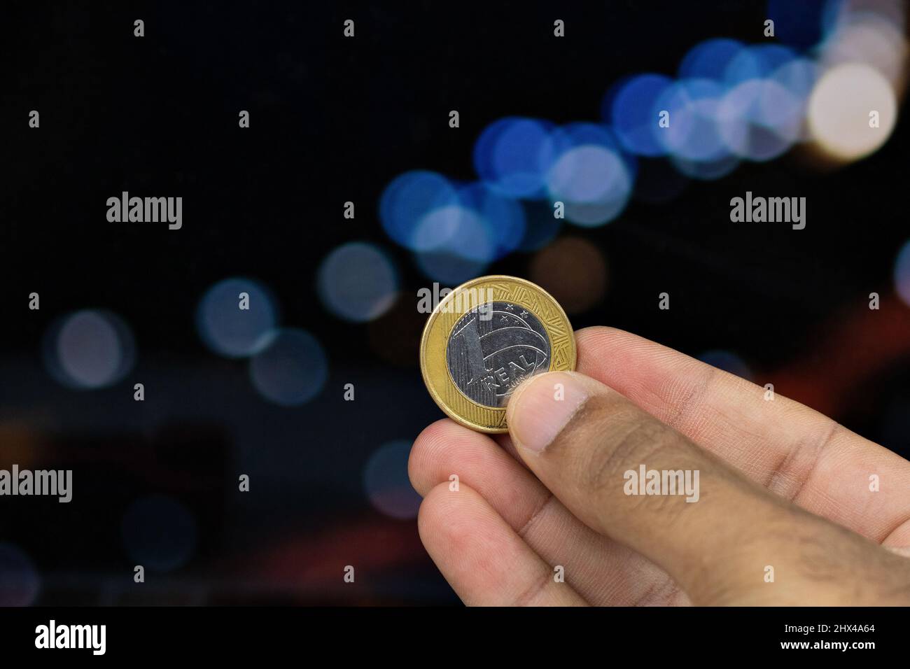 Holding a Brazilian money coin at a blurry lights background Stock ...