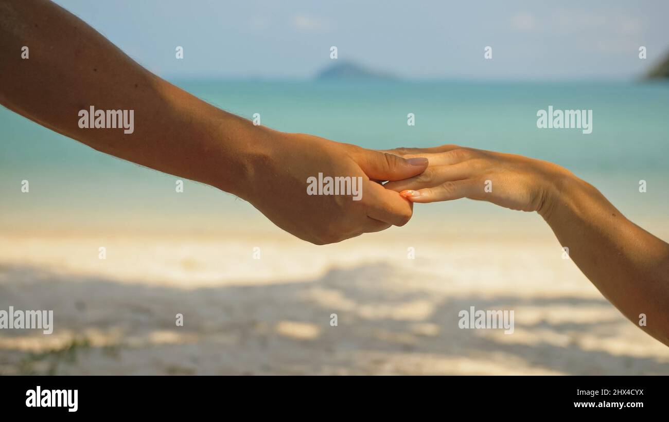 Hands of flirting young man and woman touching on beach in palms shadow ...