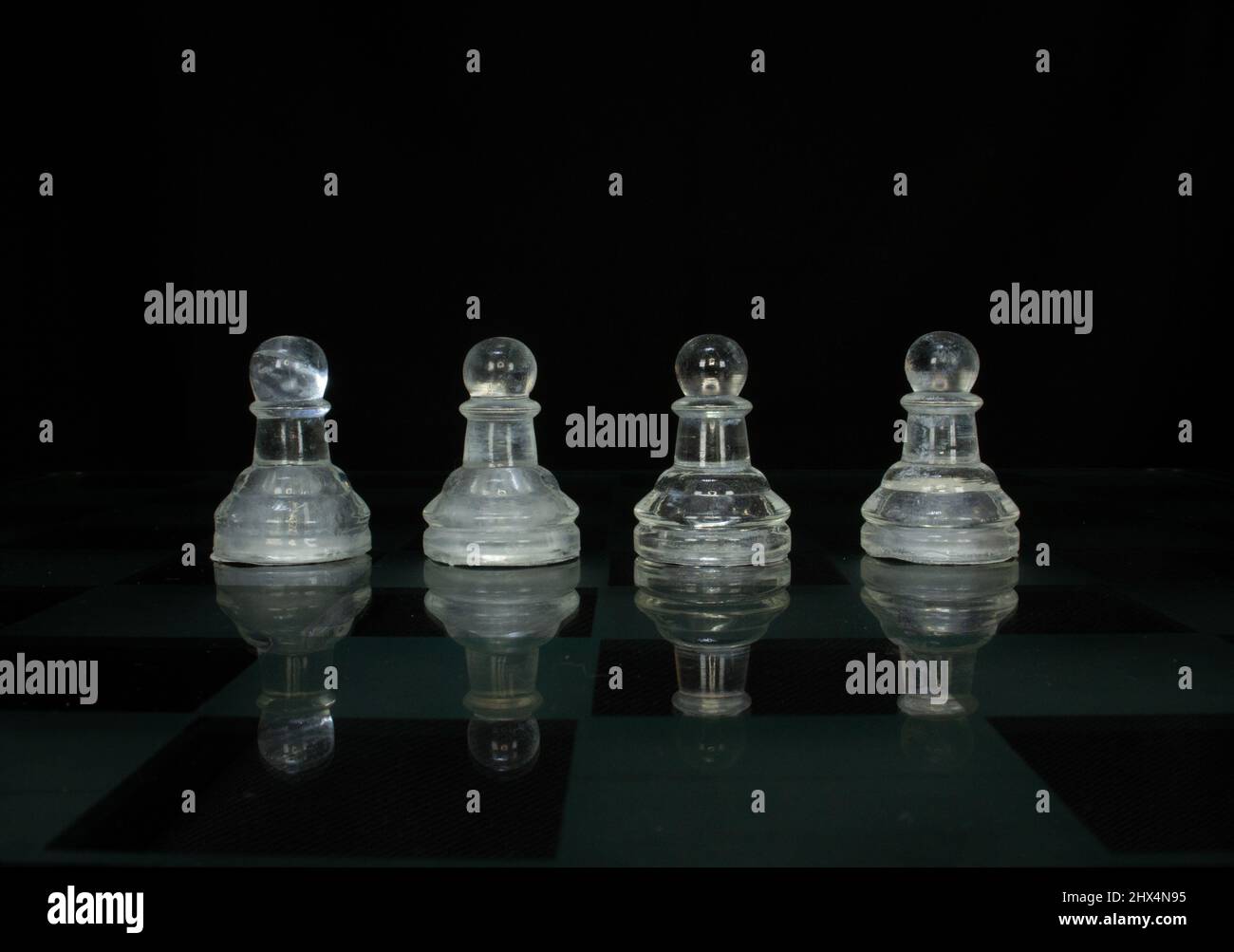 four clear chess piece pawns isolated on a chequered chess board with a ...