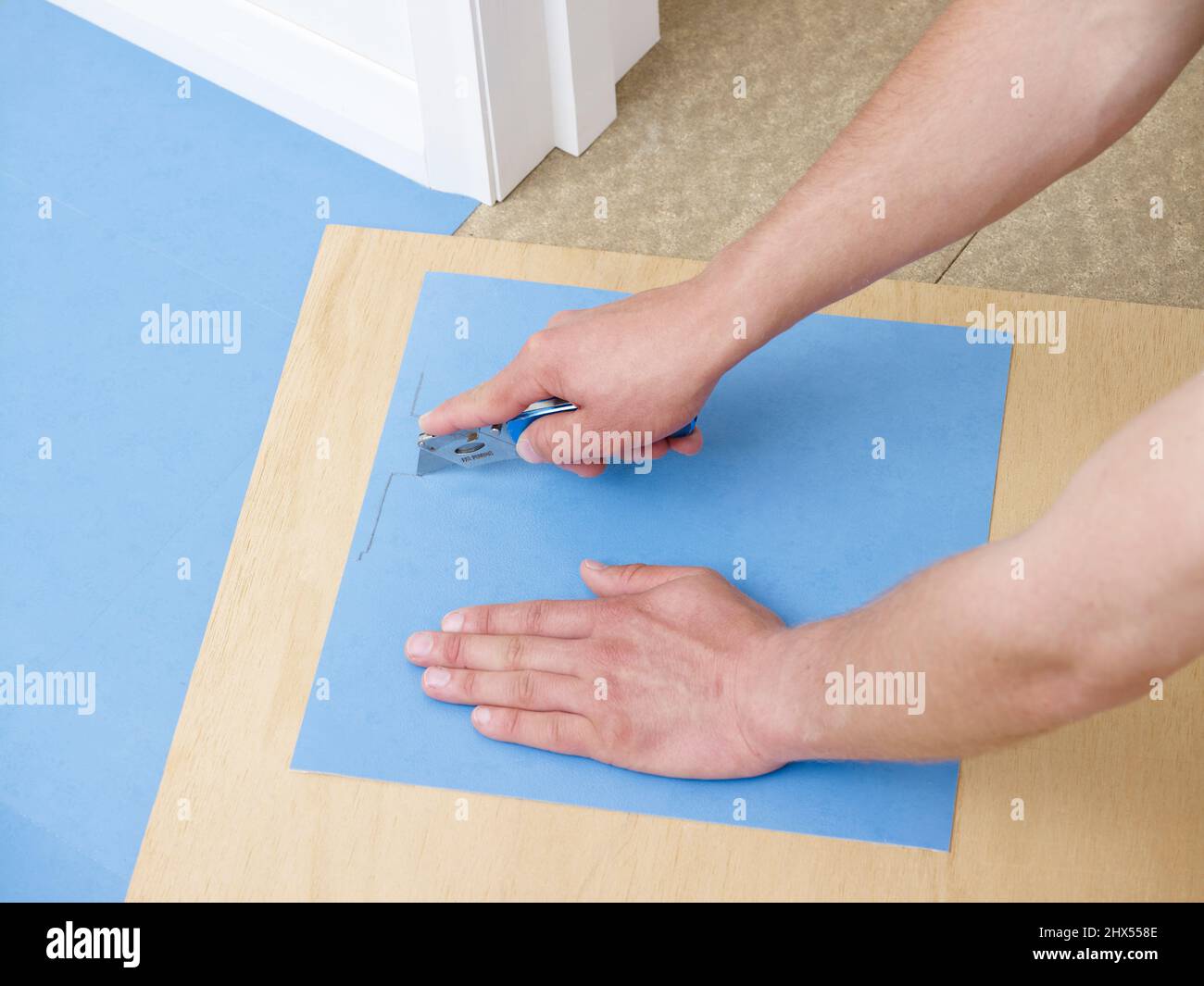 Laying vinyl tile floor, cutting tile for corner, cutting along pencil ...