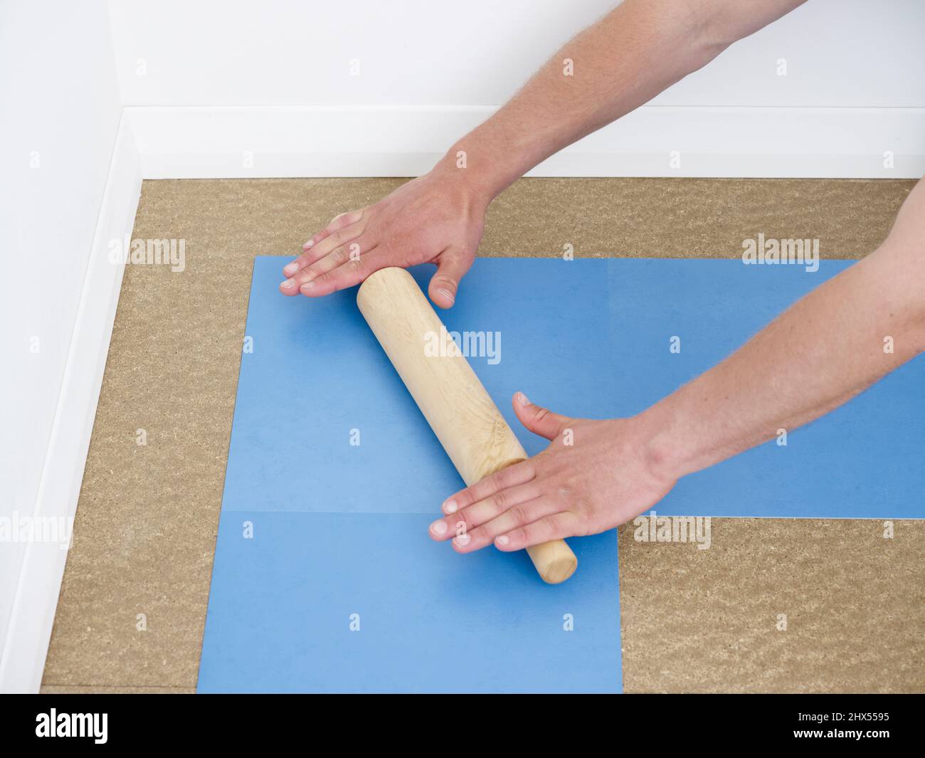 Laying vinyl tile floor, using a rolling pin to press down the tiles ...