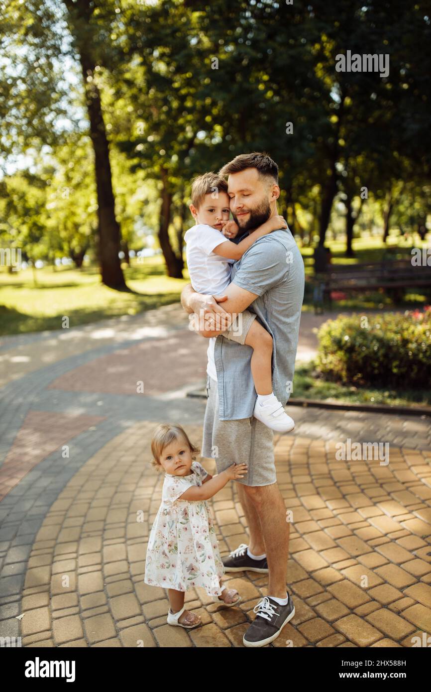 Caring dad with little kids at the park, lovely man hold in arms cute son, smiling, beautiful ...