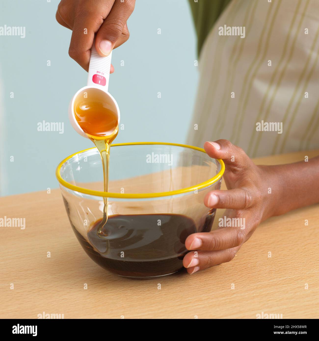 Boy adding syrup to glass mixing bowl using measuring spoon, close-up ...