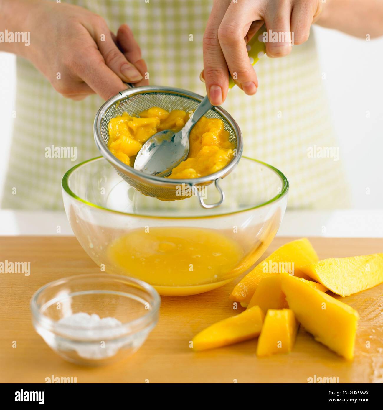 Child using spoon to squeeze juice from mango through sieve into mixing ...