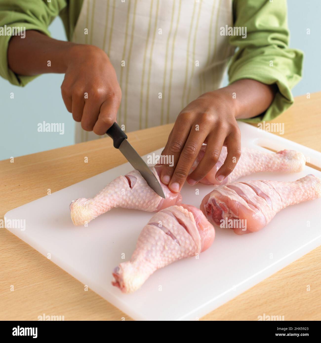 Boy slicing skin of raw chicken legs on plastic chopping board Stock ...