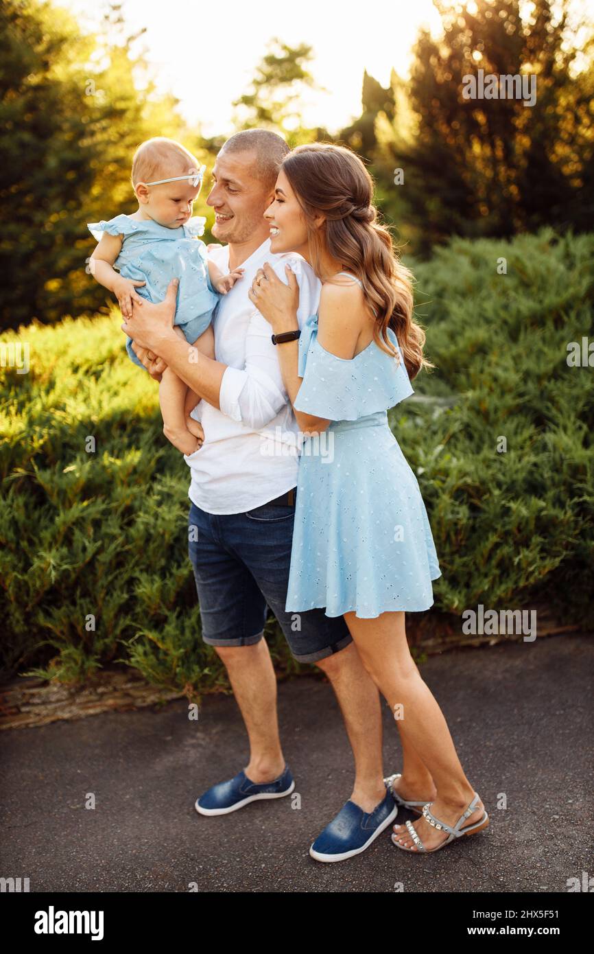 Portrait of overjoyed young family at the park, smiling parents hugging ...