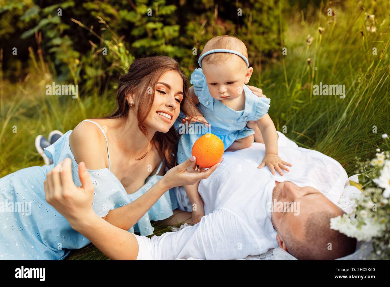 Happy young parents with adorable daughter relaxing on blanket in park ...
