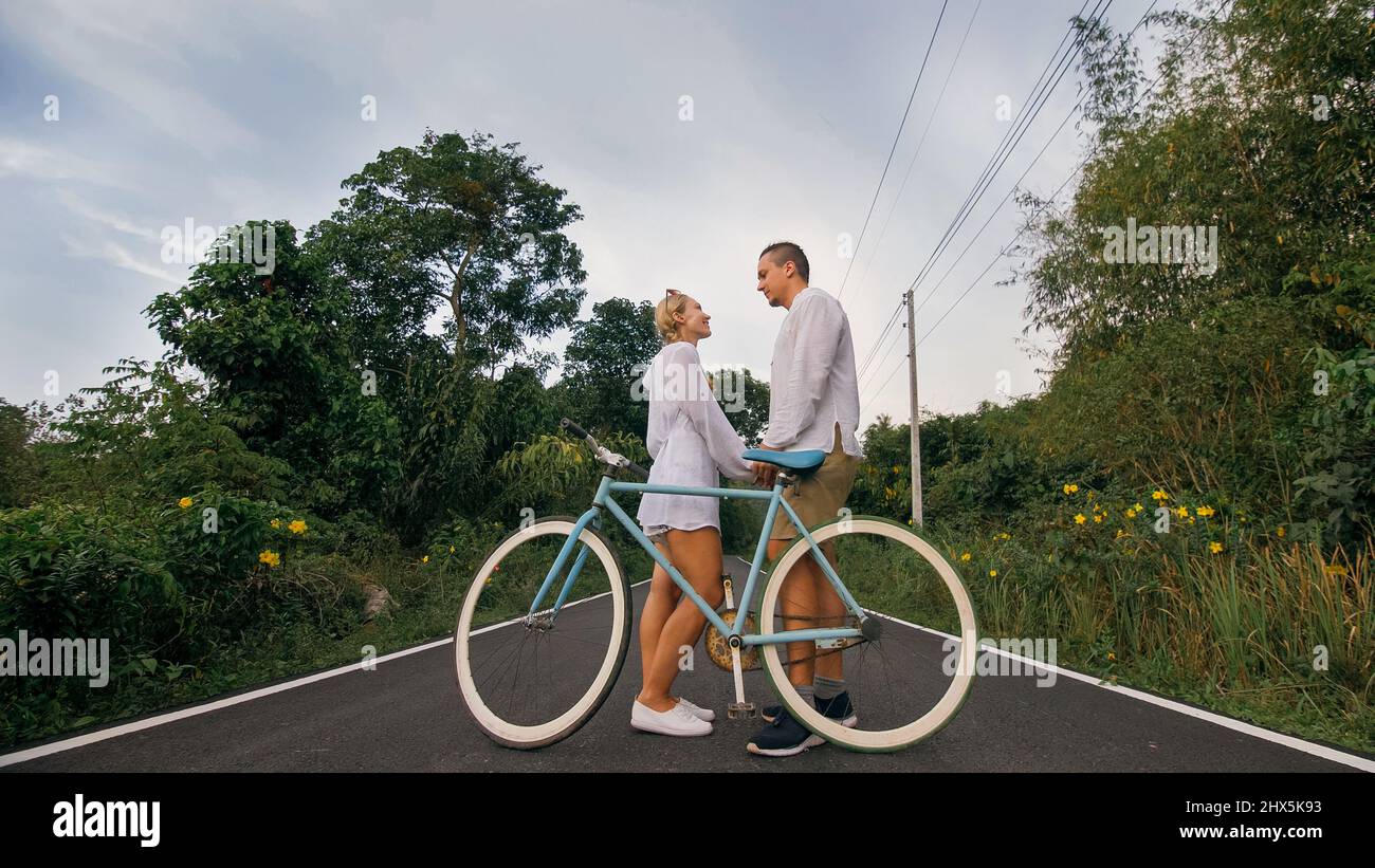Biking road trip. Love couple on blue bike in white clothes on forest road. Just married woman ...