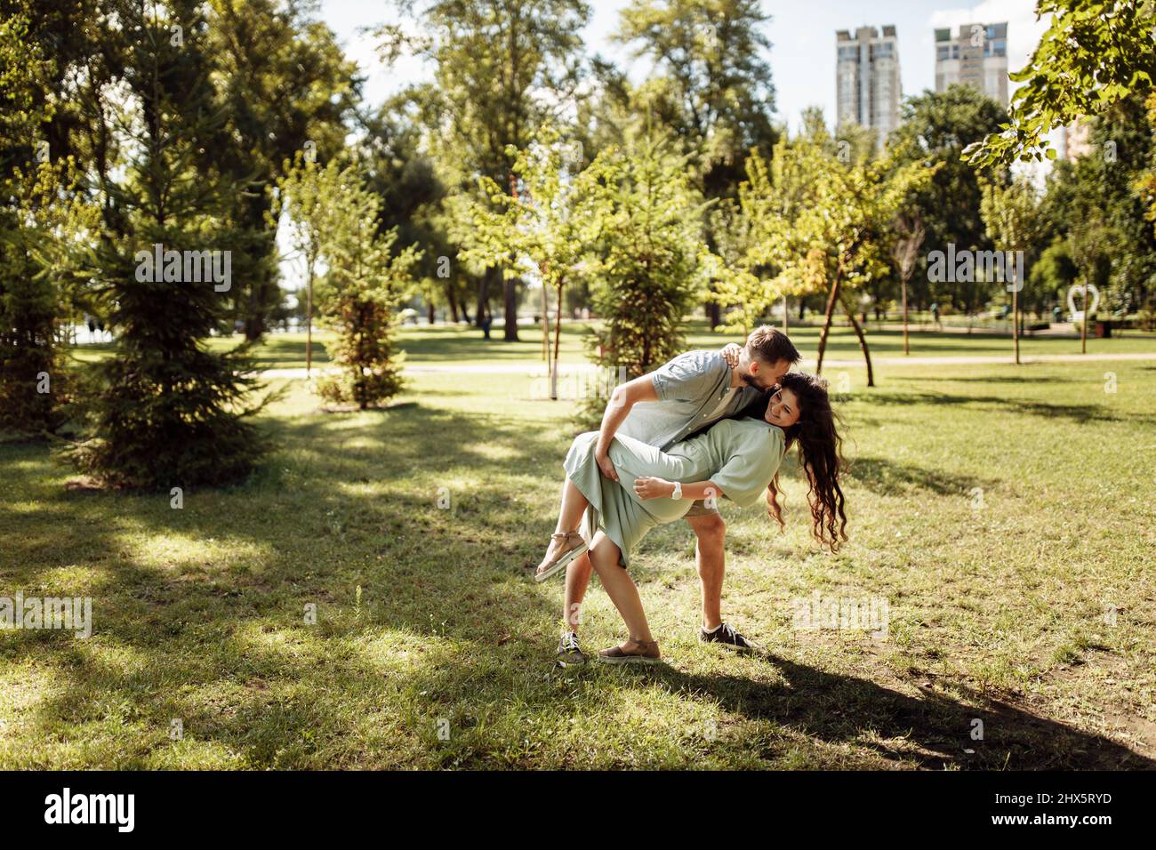 Overjoyed couple dancing at the park, loving husband hold in arms beautiful wife, pretty woman ...