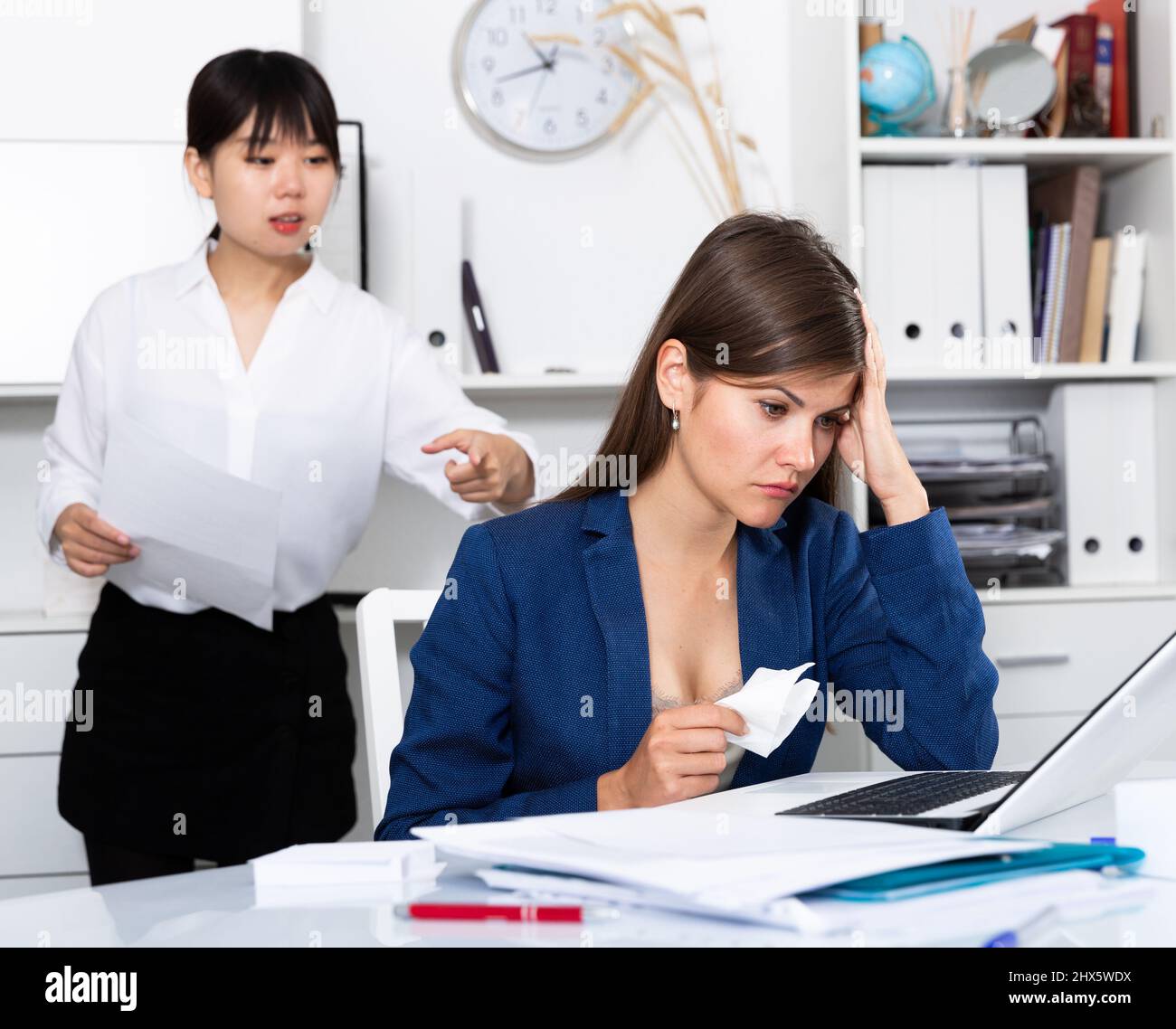 Frustrated woman sitting at office desk with disgruntled boss behind ...