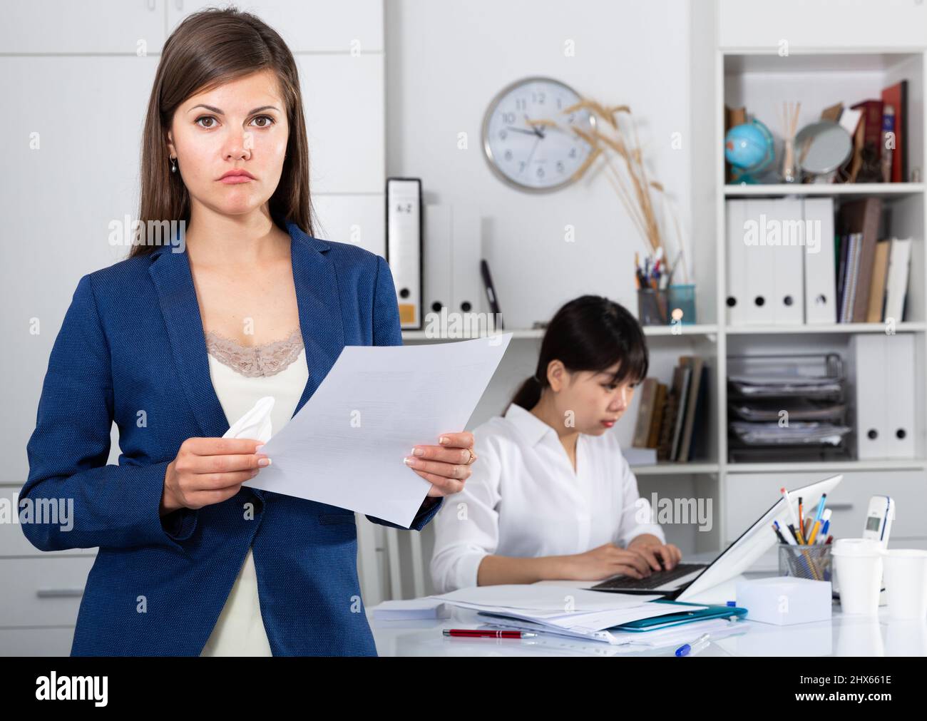 Business woman crying standing in office with working colleague behind ...