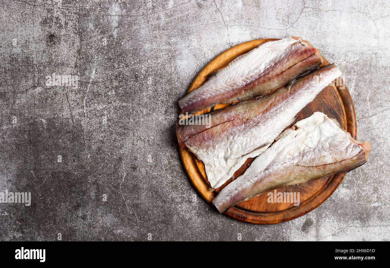 Raw Pollock (hake) fish fillet on a round wooden cutting board on a ...