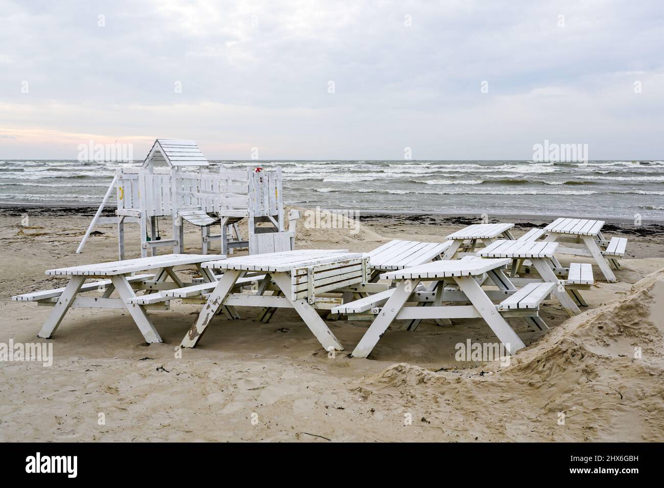 white wooden benches and tables in the sand dunes on a gray sea ...