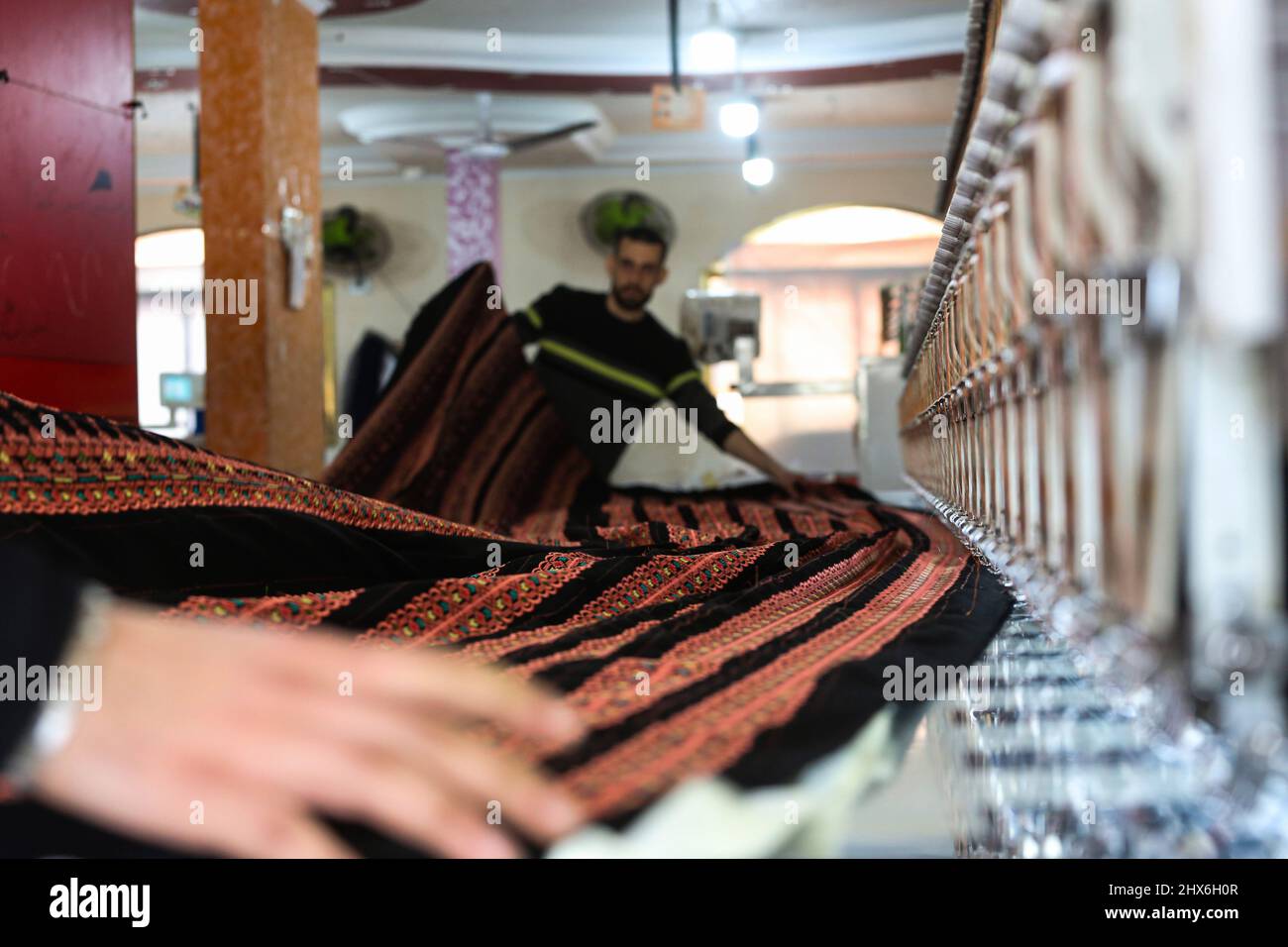 A Palestinian worker works on an embroidery machine in a sewing factory ...
