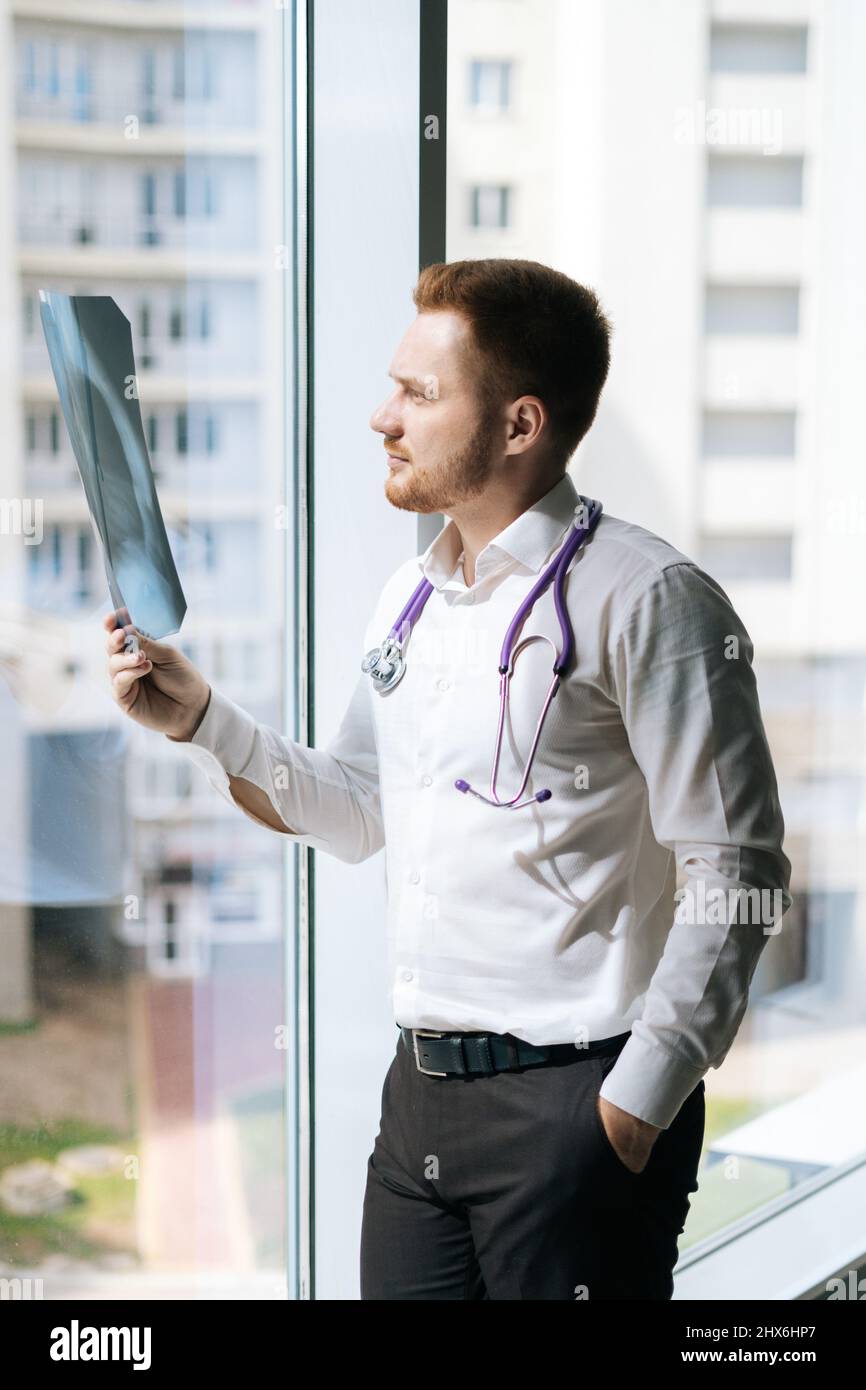 Vertical portrait of confident male doctor in white uniform examining ...