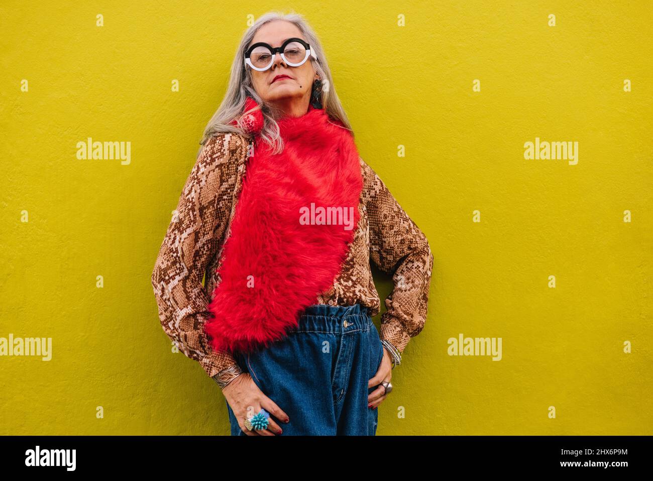 Confident senior woman standing against a lemon background. Stylish ...