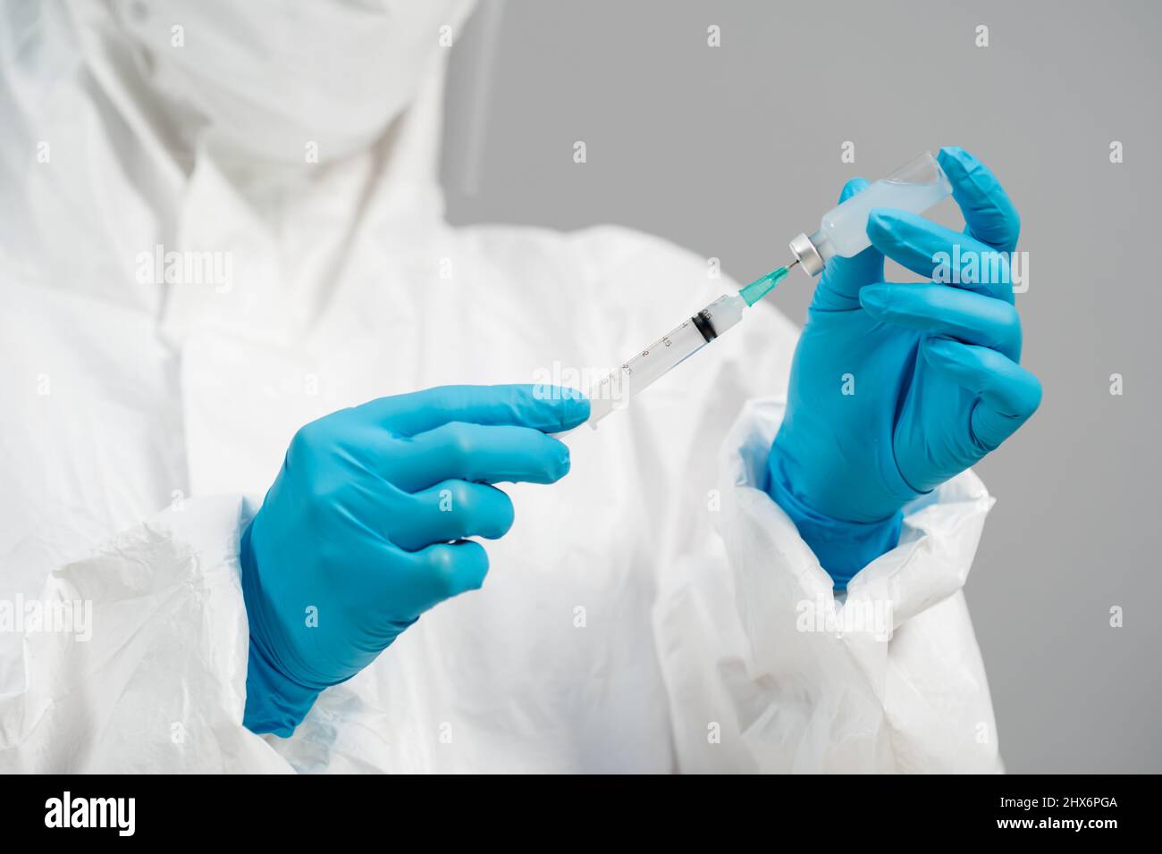 doctor in protective PPE suit drawing vaccine bottle into syringe ...