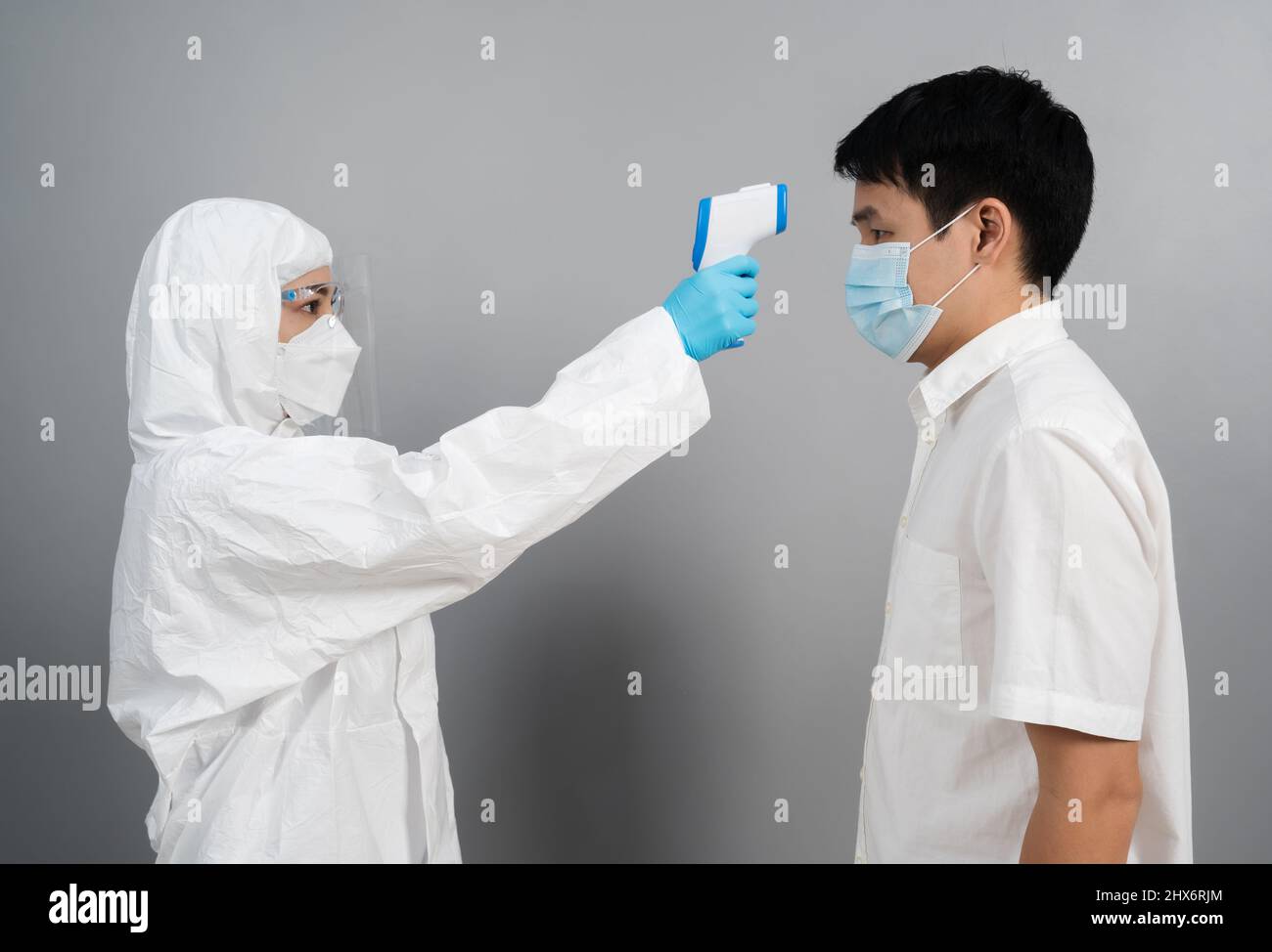 doctor in protective PPE suit using infrared thermometer measuring ...