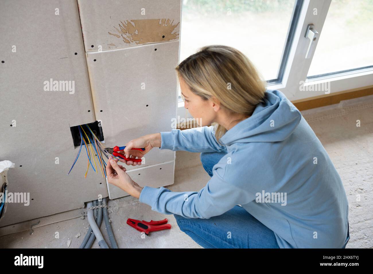 young woman with blue sweater and jeans works on electrical system on ...