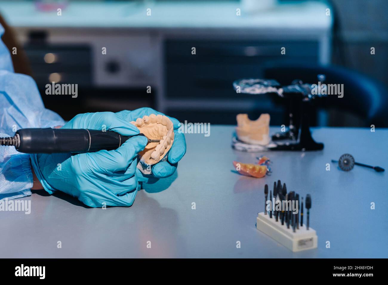 A masked and gloved dental technician works on a prosthetic tooth in ...