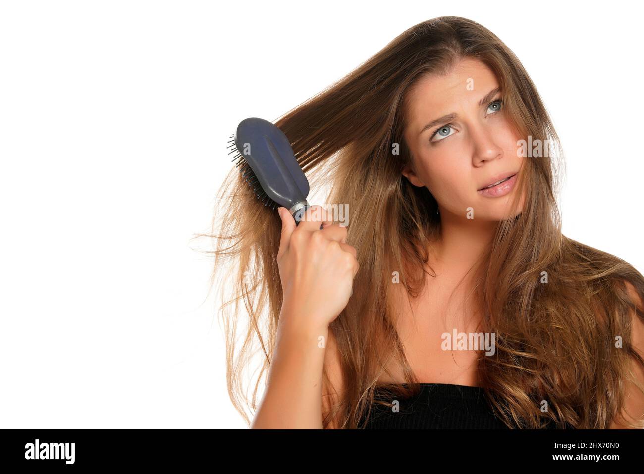 Young nervous woman brusing her hair with hairbrush on white background ...