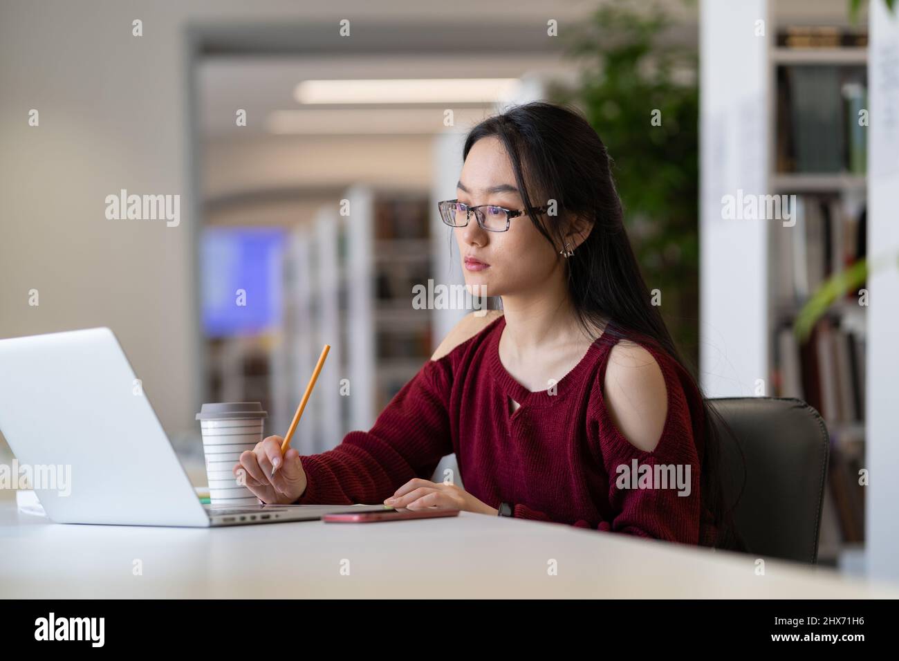 Focused chinese woman freelancer working remotely on laptop in public ...