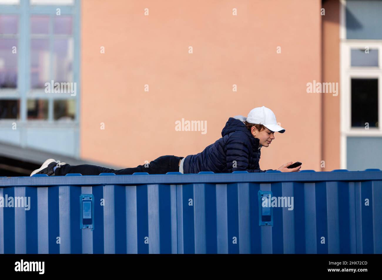 Teenage boy lying on shipping container and using cell phone Stock ...