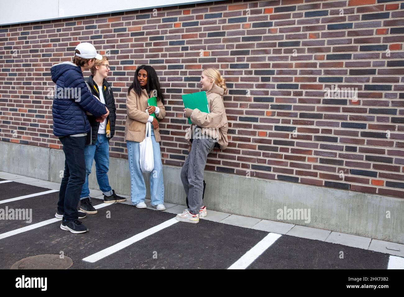 Group of students standing against brick wall and talking Stock Photo ...