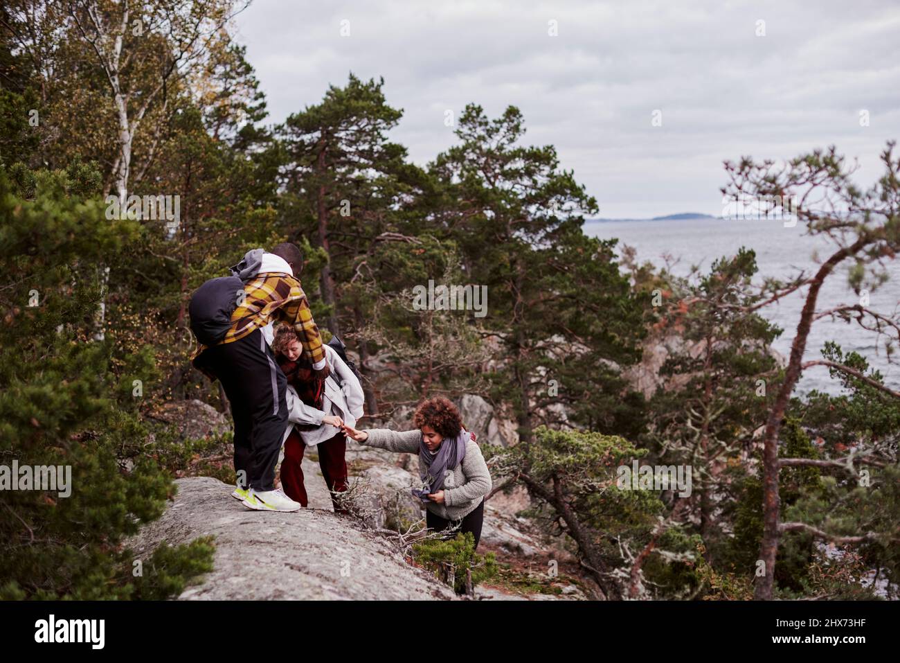 Group of friends climbing rocks on coast Stock Photo - Alamy