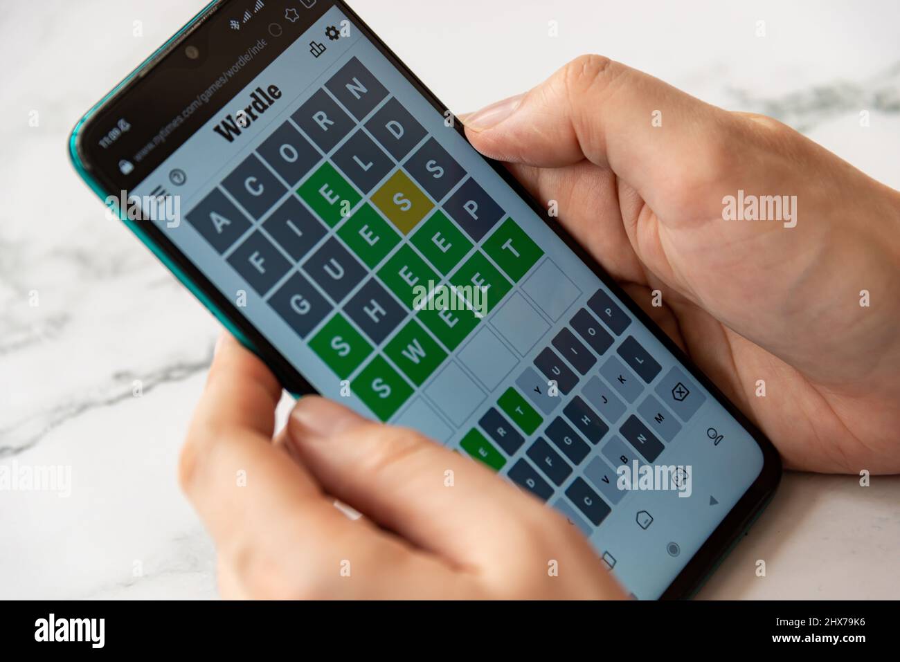 Hands playing Wordle game on phone on NYTimes.com website. Wordle is a ...
