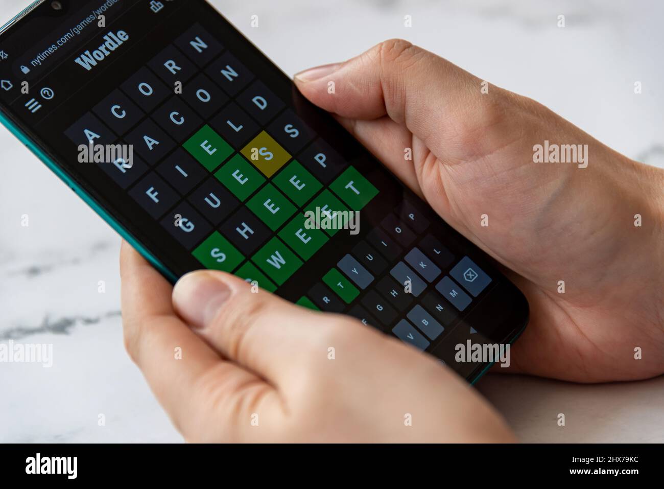 Hands playing Wordle game on phone on NYTimes.com website. Wordle is a ...
