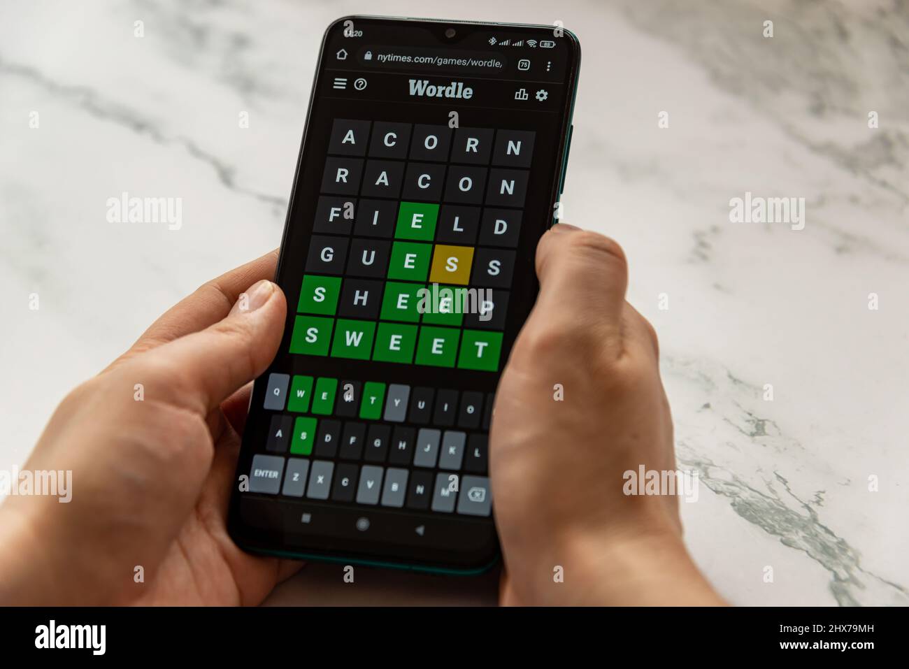 Hands playing Wordle game on phone on NYTimes.com website. Wordle is a ...