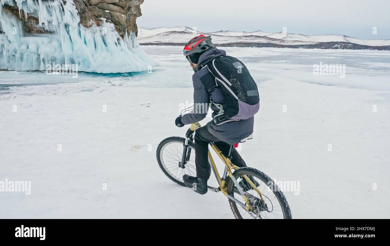 Man is riding bicycle near ice grotto. Rock with ice caves icicles ...