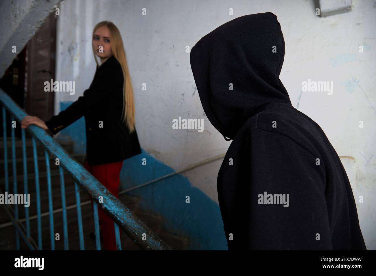 a man in a black hood chases a young woman in the entrance. the girl is ...