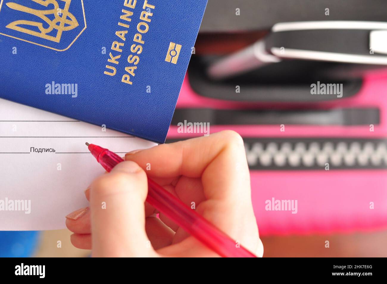 Hand with red pen signing document and Ukrainian international passport ...